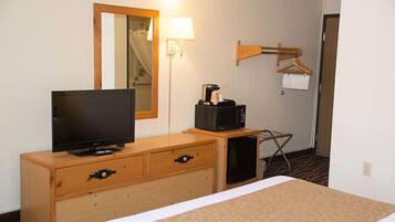 Quarto de hotel com cama, televisão sobre cômoda de madeira, micro-ondas, mesa pequena e espelho.