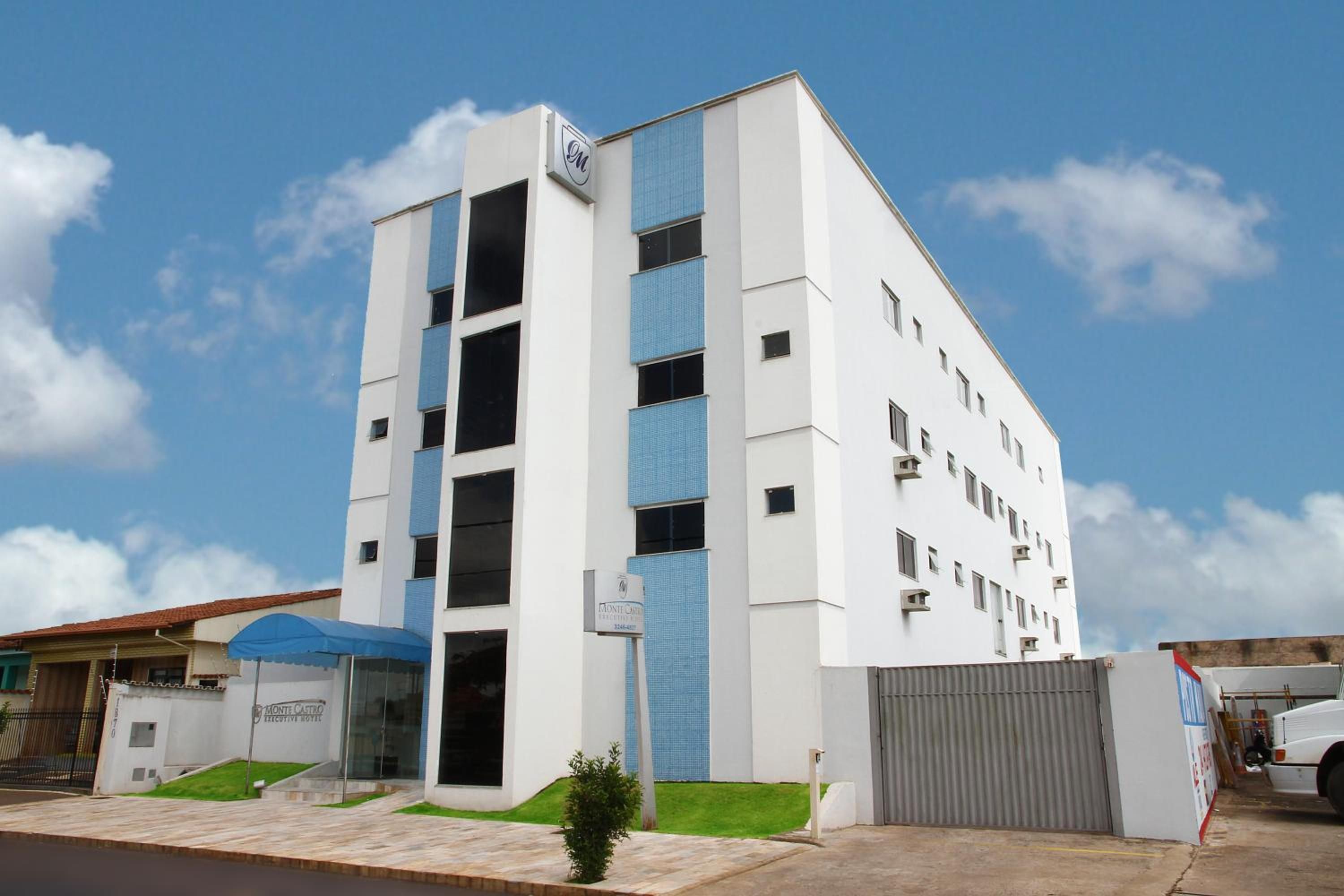Edifício de hotel moderno com fachada branca e detalhes em azul, apresentando uma entrada imponente e um acesso por portão.