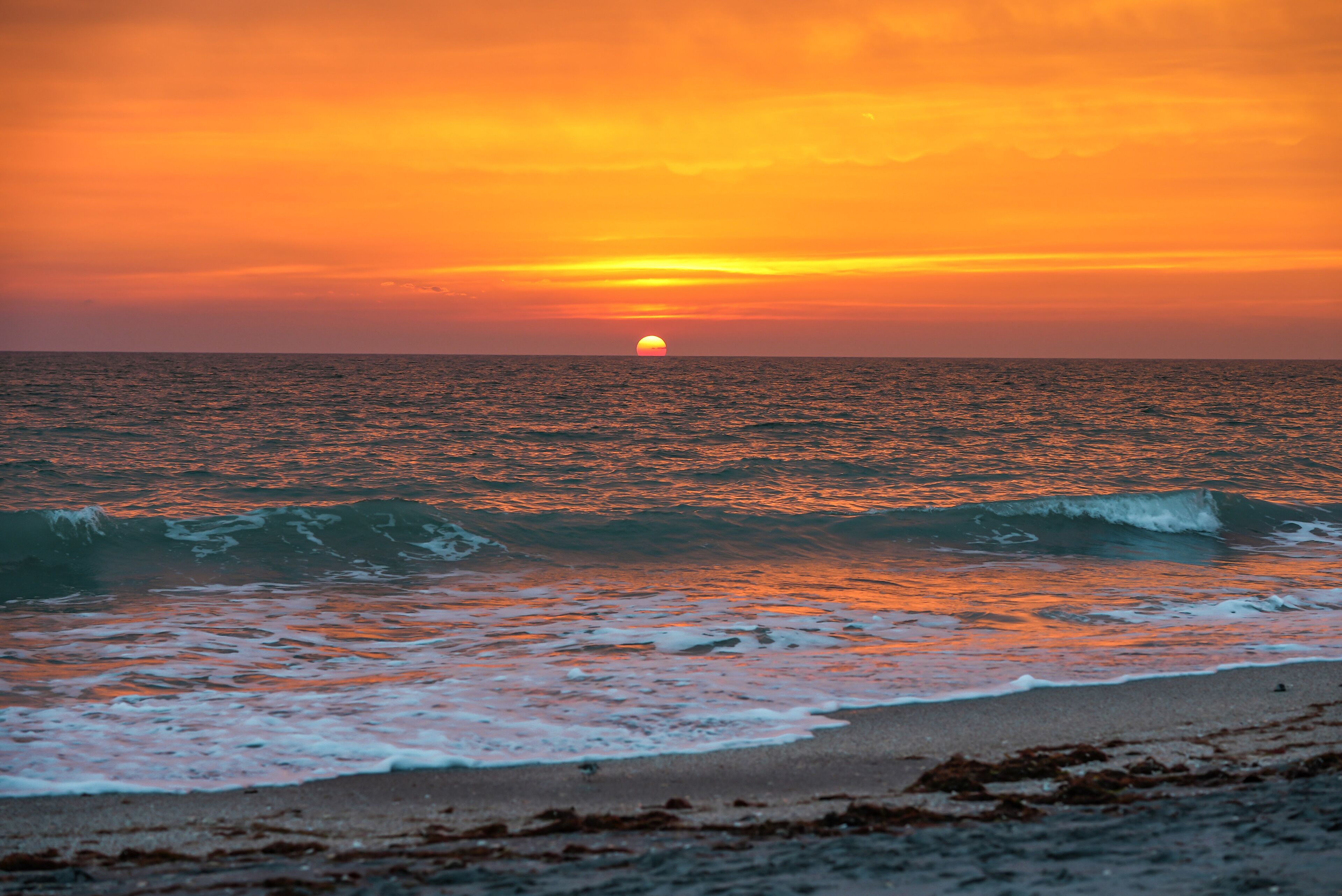 Um pôr do sol sobre o oceano com ondas se aproximando da praia.