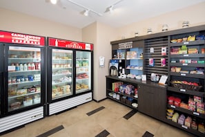 Uma loja de conveniência com áreas refrigeradas, prateleiras cheias de lanches e bebidas, e uma máquina de café.