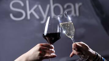 Duas mãos segurando copos de vinho, um com vinho tinto e outro com vinho branco, com um fundo exibindo a palavra "Skybar".