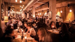 Um restaurante movimentado com dutos aparentes, lâmpadas penduradas e clientes jantando em mesas.