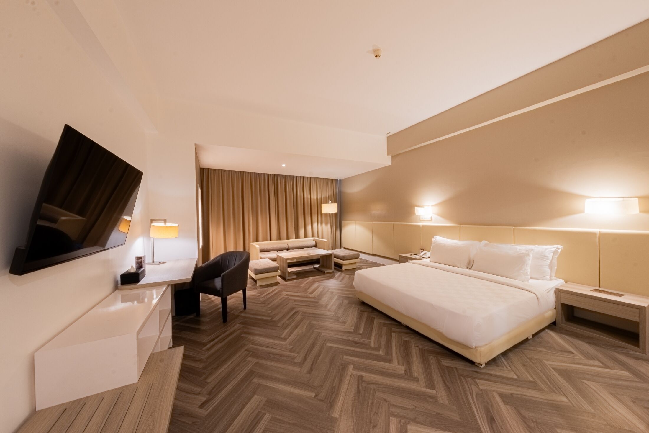 Quarto de hotel moderno com uma cama grande, uma escrivaninha, uma cadeira e uma televisão.