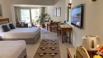 Quarto de hotel com cama, escrivaninha, cadeira, planta em vaso e televisão.