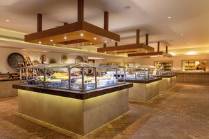 Uma área de buffet com várias estações de comida, piso estampado, teto com vigas de madeira e iluminação embutida.
