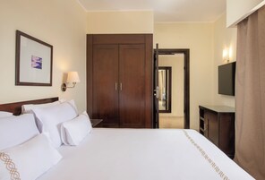 Quarto de hotel com uma cama grande, um guarda-roupa, uma mesa de cabeceira, uma lâmpada e uma televisão.
