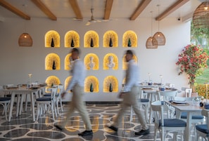 Interior de restaurante com mesas, cadeiras e arandelas decorativas na parede.