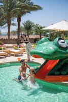 Uma piscina com um escorregador em formato de sapo, espreguiçadeiras e palmeiras ao fundo.