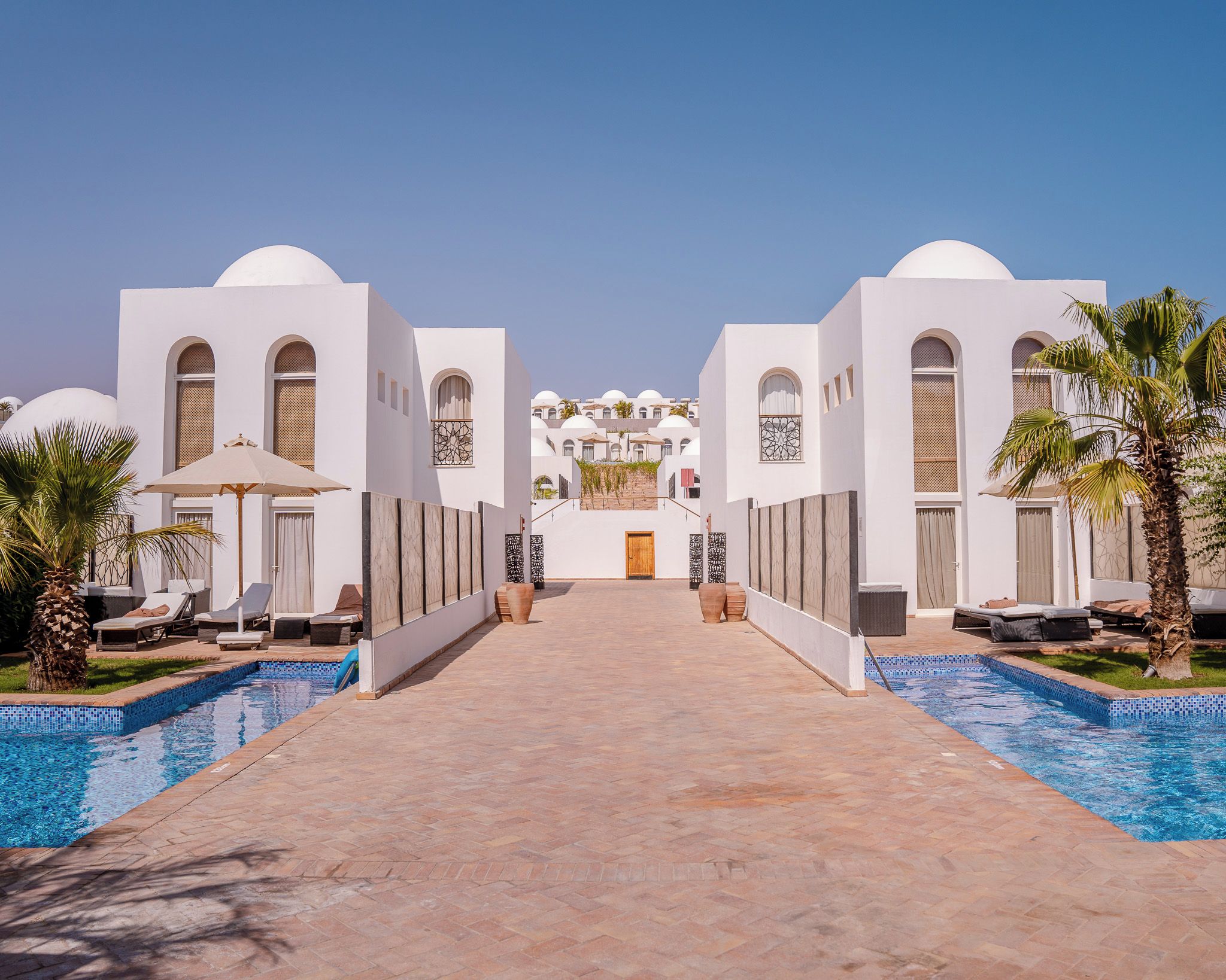 Um resort com piscina central, áreas de estar e vista para os edifícios do resort ao longe.