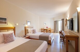 Quarto de hotel com duas camas, uma mesa, uma cadeira, televisão e janela com cortinas.