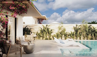 Uma área à beira da piscina com espreguiçadeiras, uma mesa de jantar e um espaço de estar com vista para a piscina.
