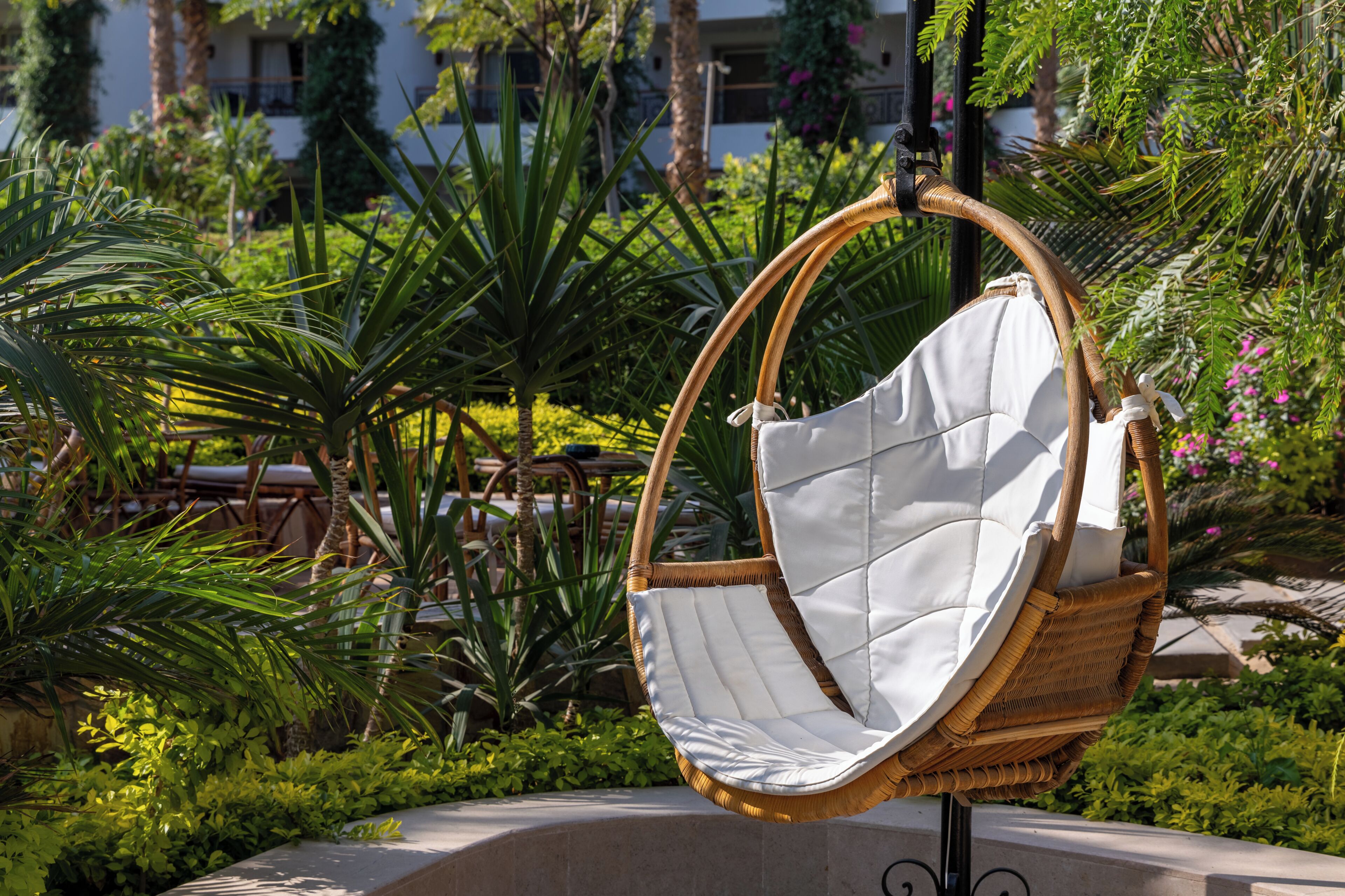 Uma cadeira suspensa de vime com almofada branca em um jardim exuberante.