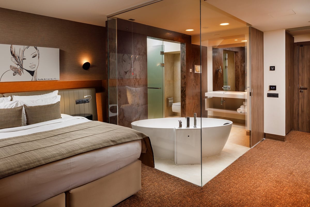 Quarto de hotel moderno com uma cama grande, uma banheira independente e área de chuveiro com paredes de vidro.