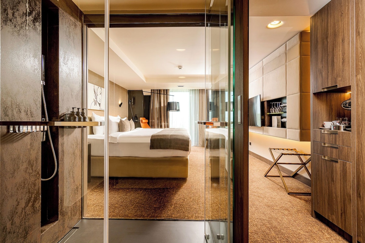 Quarto de hotel moderno com uma cama grande, área de estar e minibar.