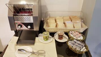 Uma mesa de café da manhã com torradeira, pão, manteiga, geleia e acompanhamentos.