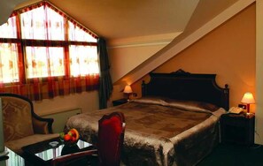 Quarto com cama, cadeira, mesa de cabeceira com abajur e janela com cortinas.