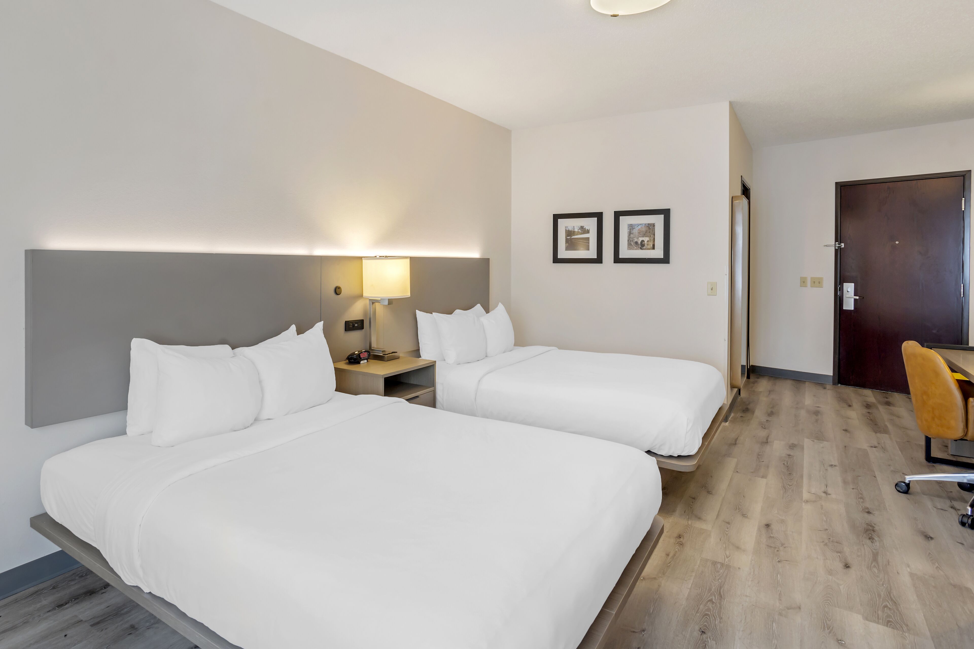 Quarto de hotel com duas camas, uma escrivaninha, uma cadeira e uma porta.