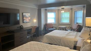 Quarto de hotel com duas camas, uma escrivaninha com cadeira, televisão e um quadro na parede.