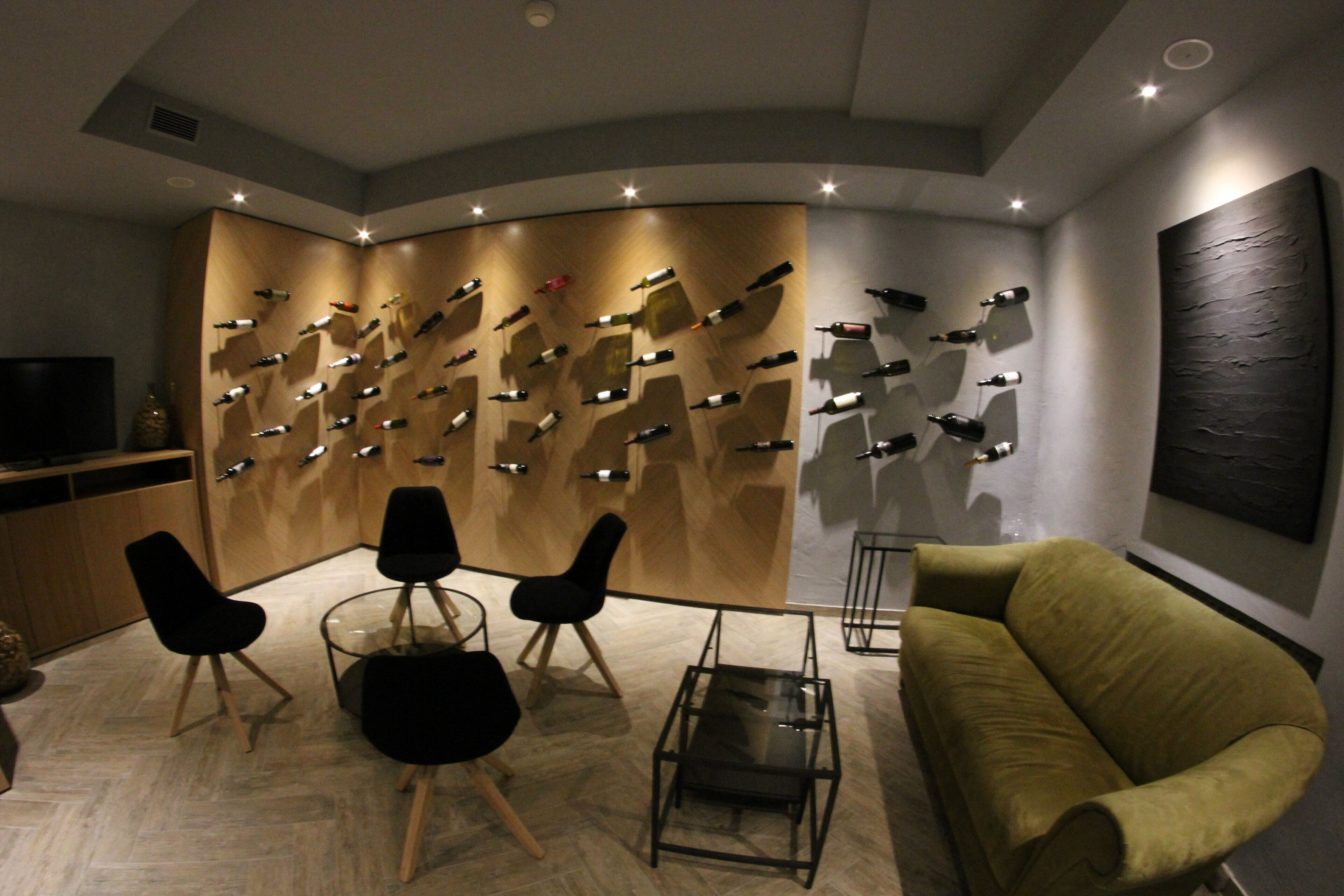 Um interior moderno com um espaço para vinhos fixado na parede, um sofá verde e uma mesa de vidro com cadeiras.