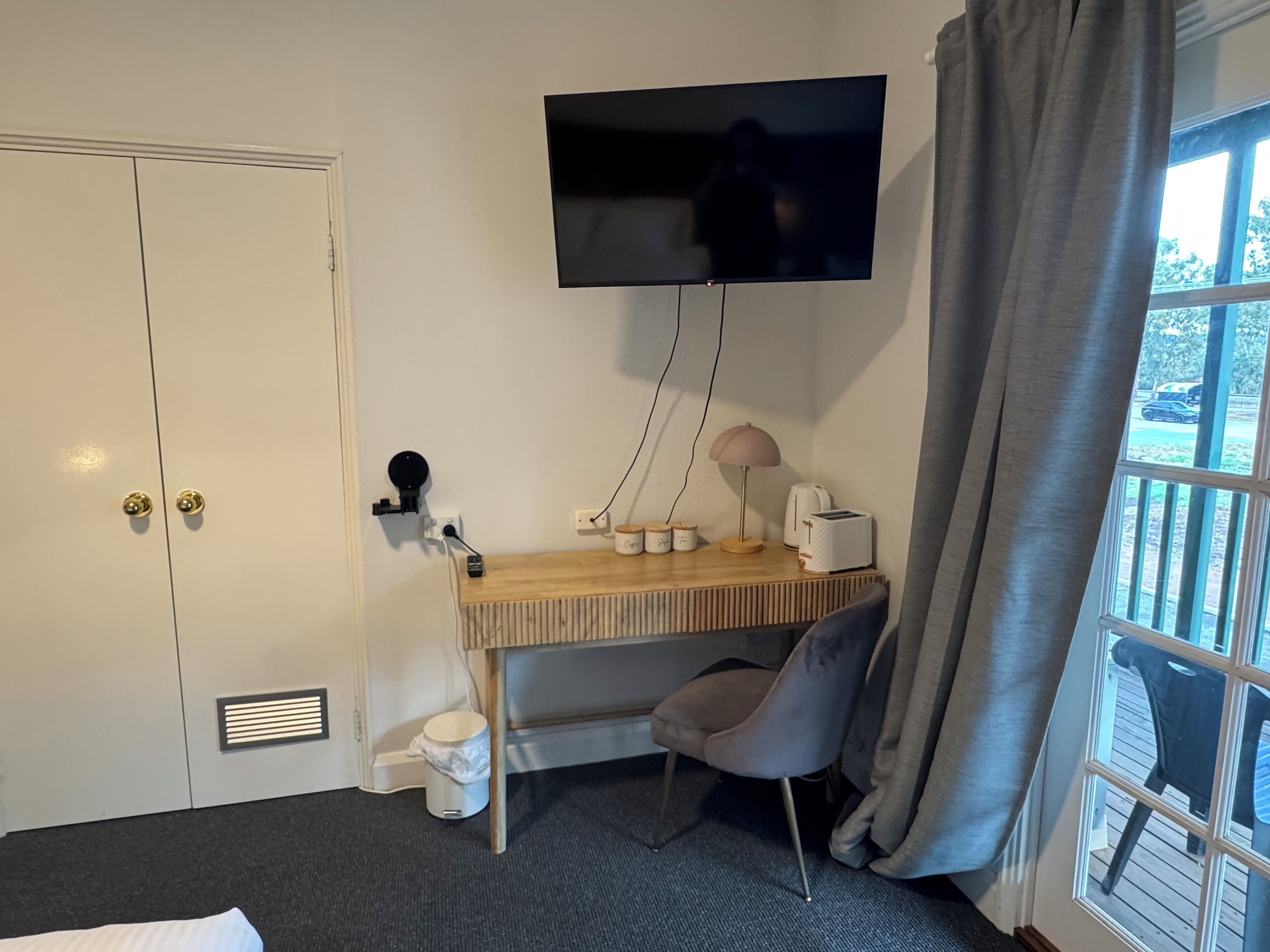 Quarto de hotel com uma cama, uma escrivaninha com TV de tela plana, uma cadeira, uma janela com cortinas e vista para o exterior.