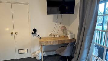 Quarto de hotel com uma cama, uma escrivaninha com TV de tela plana, uma cadeira, uma janela com cortinas e vista para o exterior.