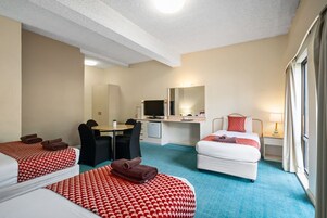 Quarto de hotel com duas camas, uma escrivaninha, uma cadeira, uma televisão e uma janela com cortinas.