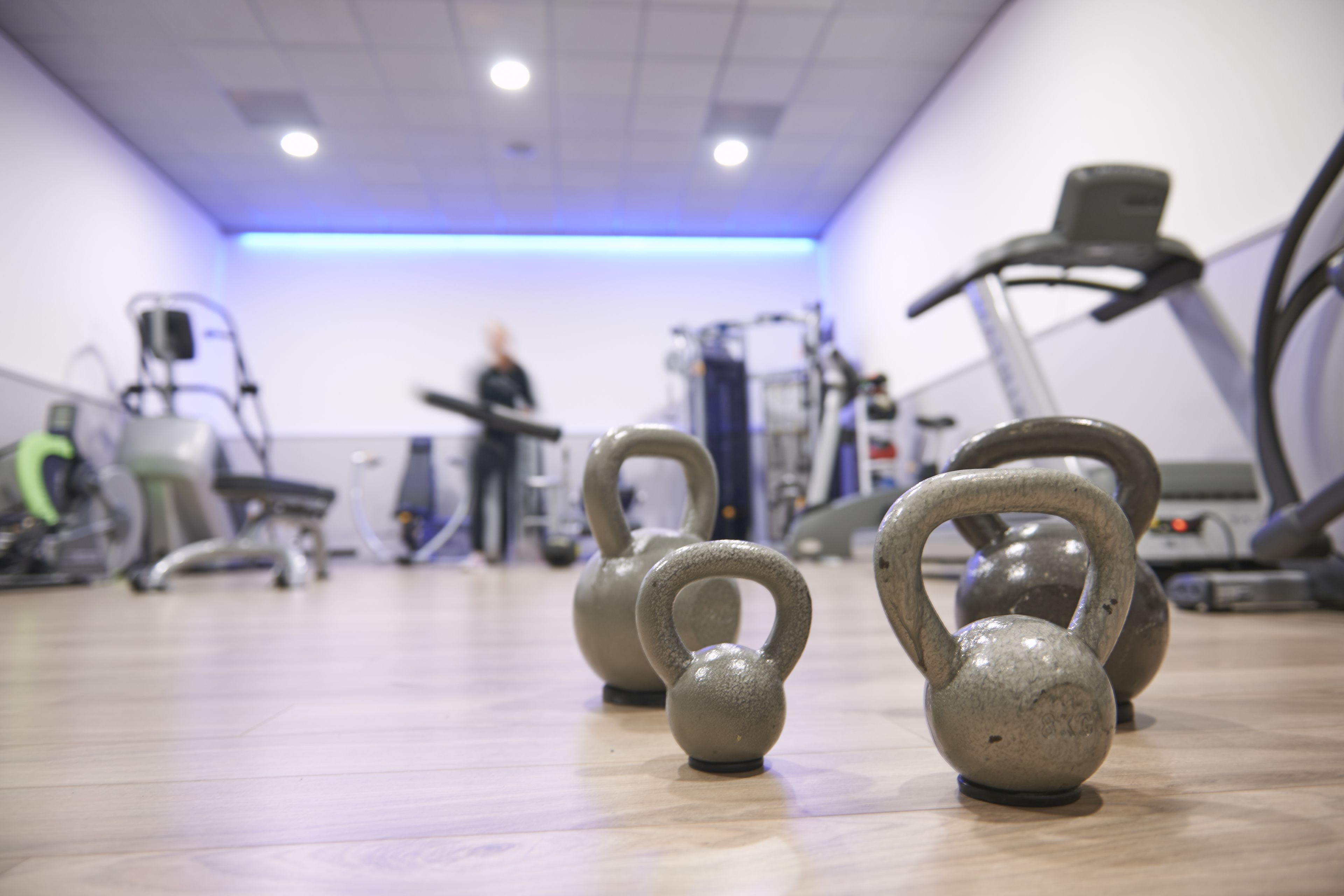 Uma academia com halteres em primeiro plano e equipamentos de exercício ao fundo.