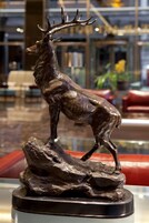 Escultura de bronze de um veado em pedestal em um saguão com assentos de couro e divisórias de vidro.