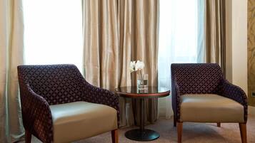 Duas poltronas estampadas com uma mesa de vidro entre elas, um vaso com flores brancas e uma vista através de cortinas bege.