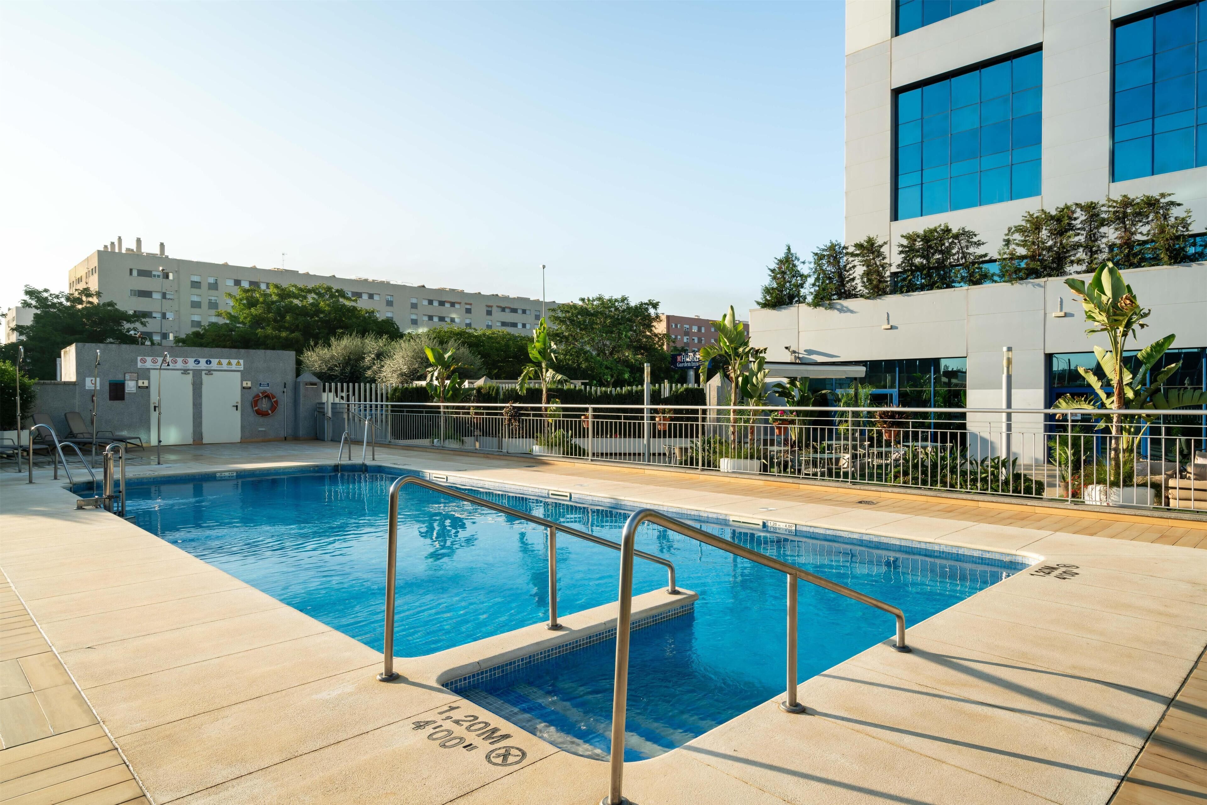 Uma piscina com um posto de salva-vidas, uma cerca e um edifício com grandes janelas ao fundo.