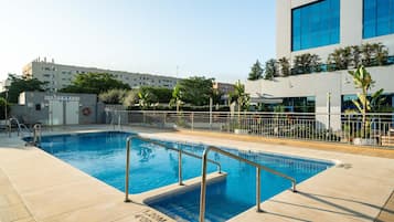 Uma piscina com um posto de salva-vidas, uma cerca e um edifício com grandes janelas ao fundo.