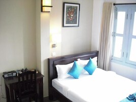 Quarto de hotel com cama, escrivaninha e janela.