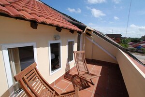 Uma casa pequena com telhado de telhas e varanda com cadeiras de madeira.