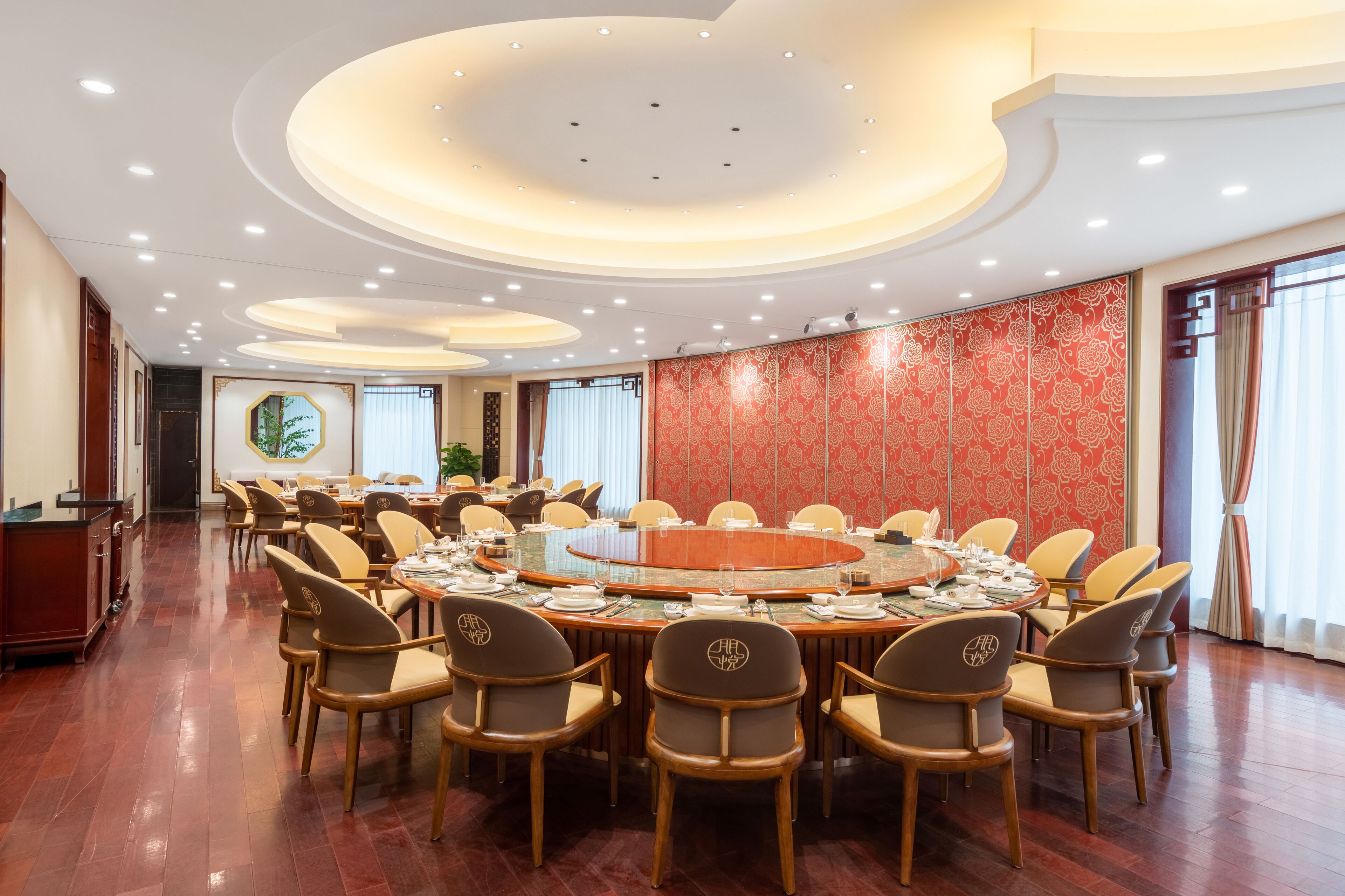 Uma sala de conferência com uma mesa redonda, várias cadeiras e um amplo janelão com cortinas.