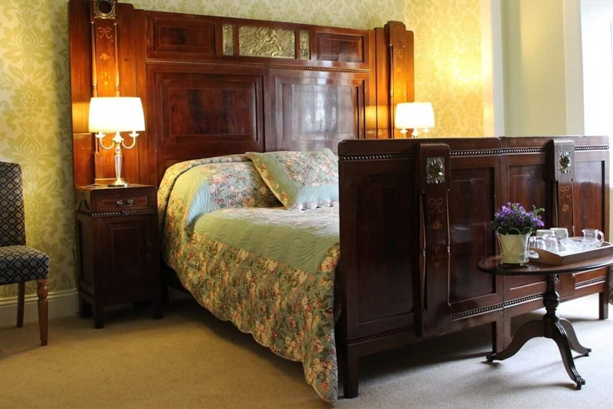 Uma cama de madeira clássica com dossel, roupa de cama floral, duas luminárias de cabeceira e uma mesinha de cabeceira com abajur.