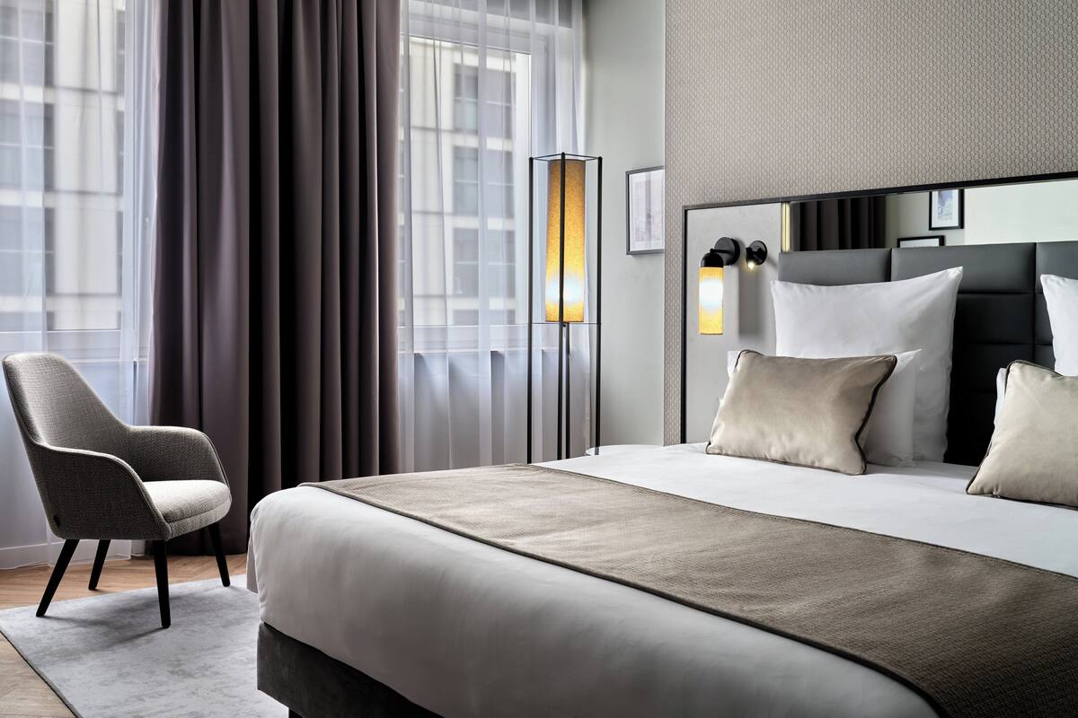 Quarto de hotel moderno com uma cama grande, uma cadeira e um abajur.