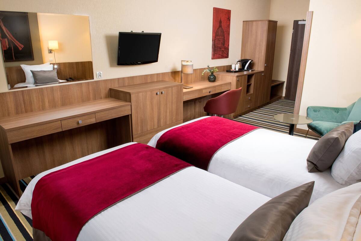 Quarto de hotel com duas camas, uma mesa, uma cadeira, uma televisão e um guarda-roupa.