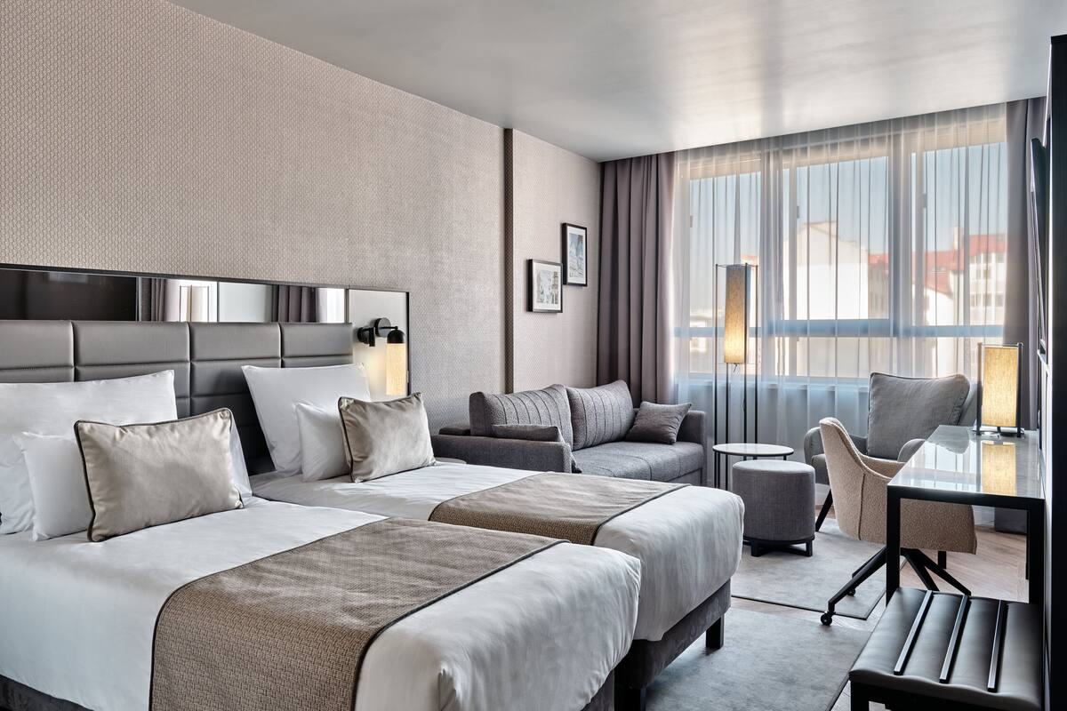 Quarto de hotel com duas camas, um sofá, uma escrivaninha e uma cadeira.