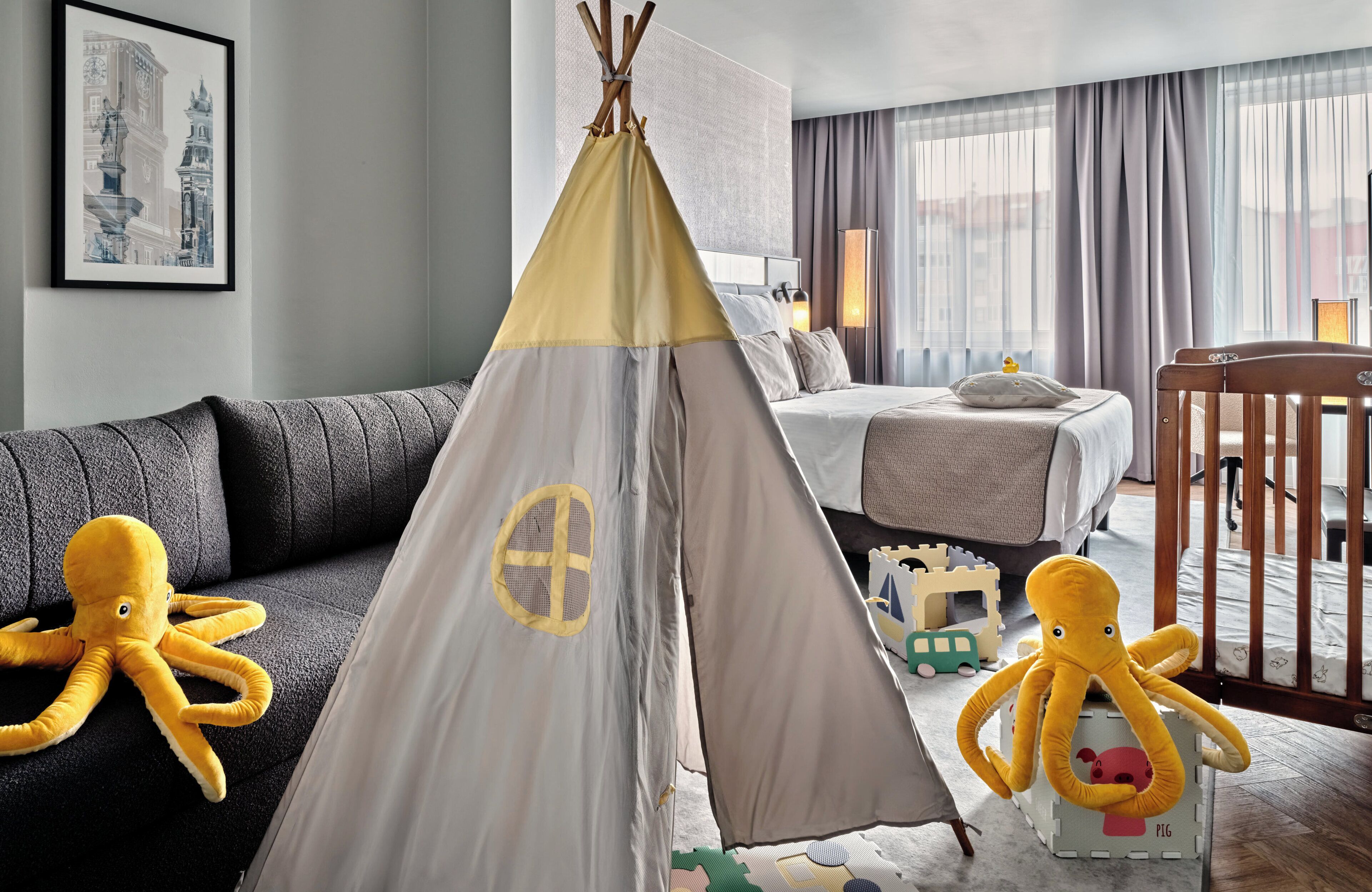 Quarto de hotel com cama, sofá, tenda e brinquedos.
