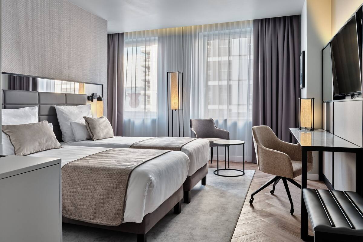 Quarto de hotel com duas camas, uma escrivaninha, uma cadeira e uma televisão.