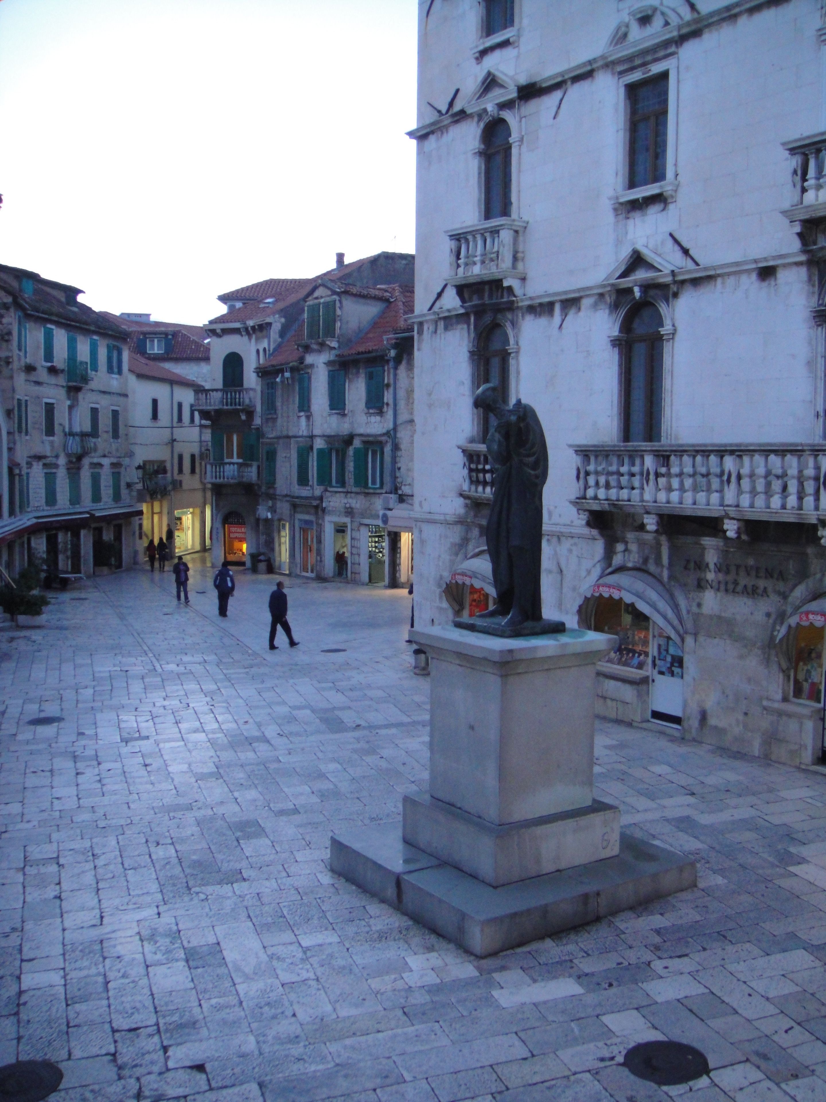 Um pátio com uma estátua, edifícios com varandas e chão pavimentado.