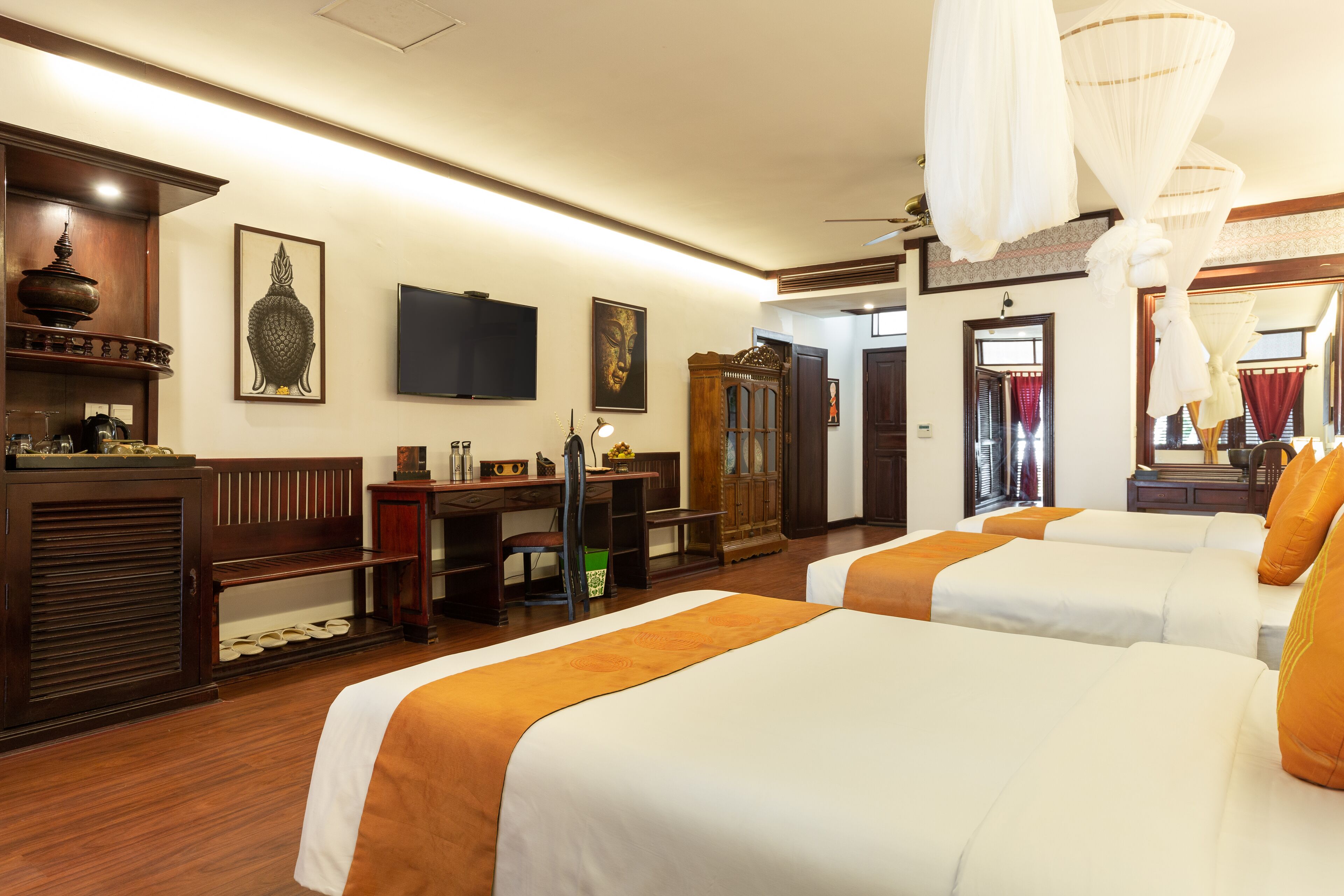 Quarto de hotel com duas camas, uma escrivaninha, uma televisão e um guarda-roupa.