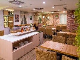 Restaurante com parede de tijolos, cadeiras de vime e um espaço para buffet.