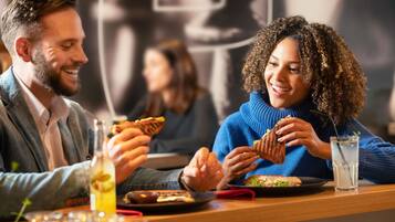Um casal jantando em um restaurante com ambiente informal, incluindo uma mesa com bebida e sanduíche.