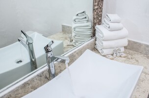 Casa de banho com banheira, pia e espelho. Toalhas dobradas e artigos de higiene pessoal estão no balcão.