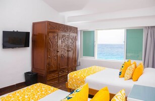 Quarto de hotel com duas camas, televisão, guarda-roupa de madeira e janela com vista para o mar.