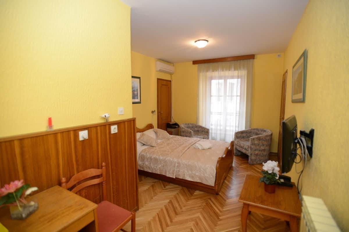 Quarto com cama, duas cadeiras, escrivaninha e televisão.