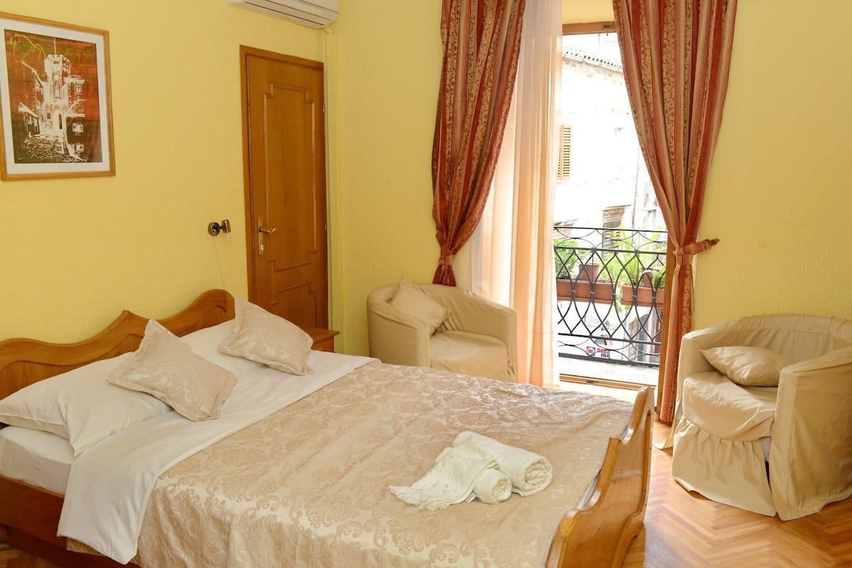 Quarto com cama, cadeira, porta e varanda com guarda-corpo.