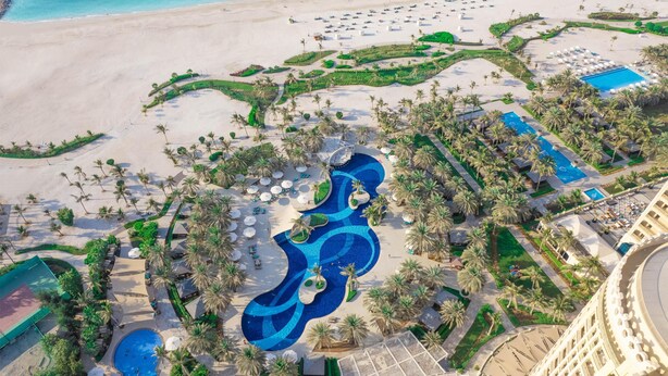 Vista aérea de um resort com uma piscina grande, área de praia e palmeiras.