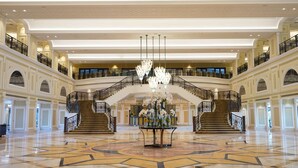 Um hall imponente com um lustre central, várias escadarias e um piso de mármore polido.